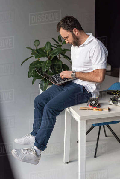 Man sitting on table and using laptop - Royalty-free Stock Photo | Dissolve