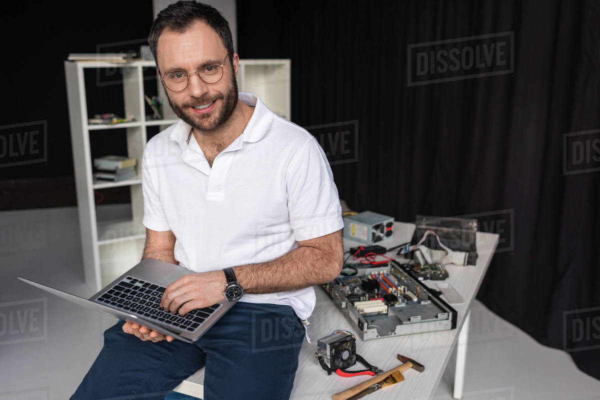 Smiling man sitting on table and using laptop - Royalty-free Stock ...
