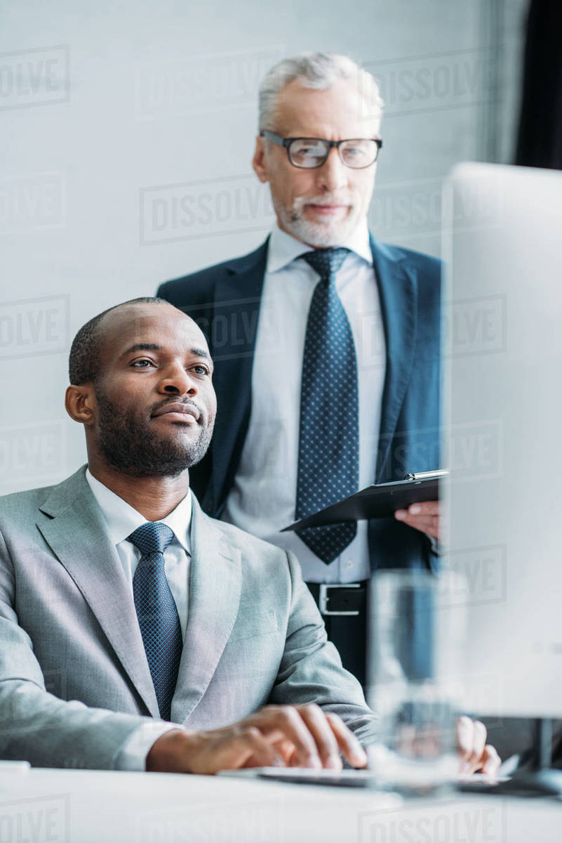Multiethnic business colleagues looking at computer screen at workplace ...