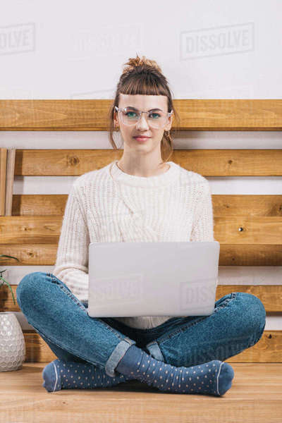 Girl sitting on table in office with laptop and looking at camera ...