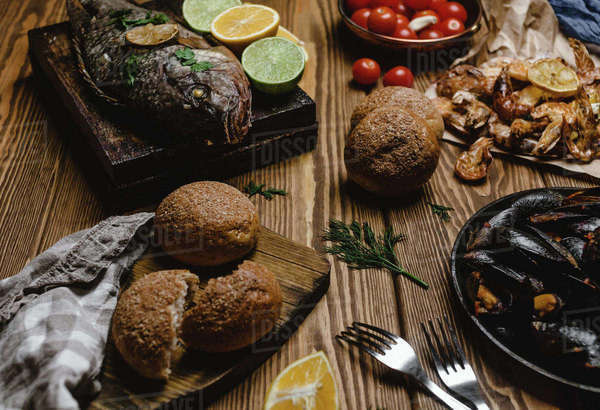 Assorted seafood and baked fish with bread and tomatoes on wooden table ...