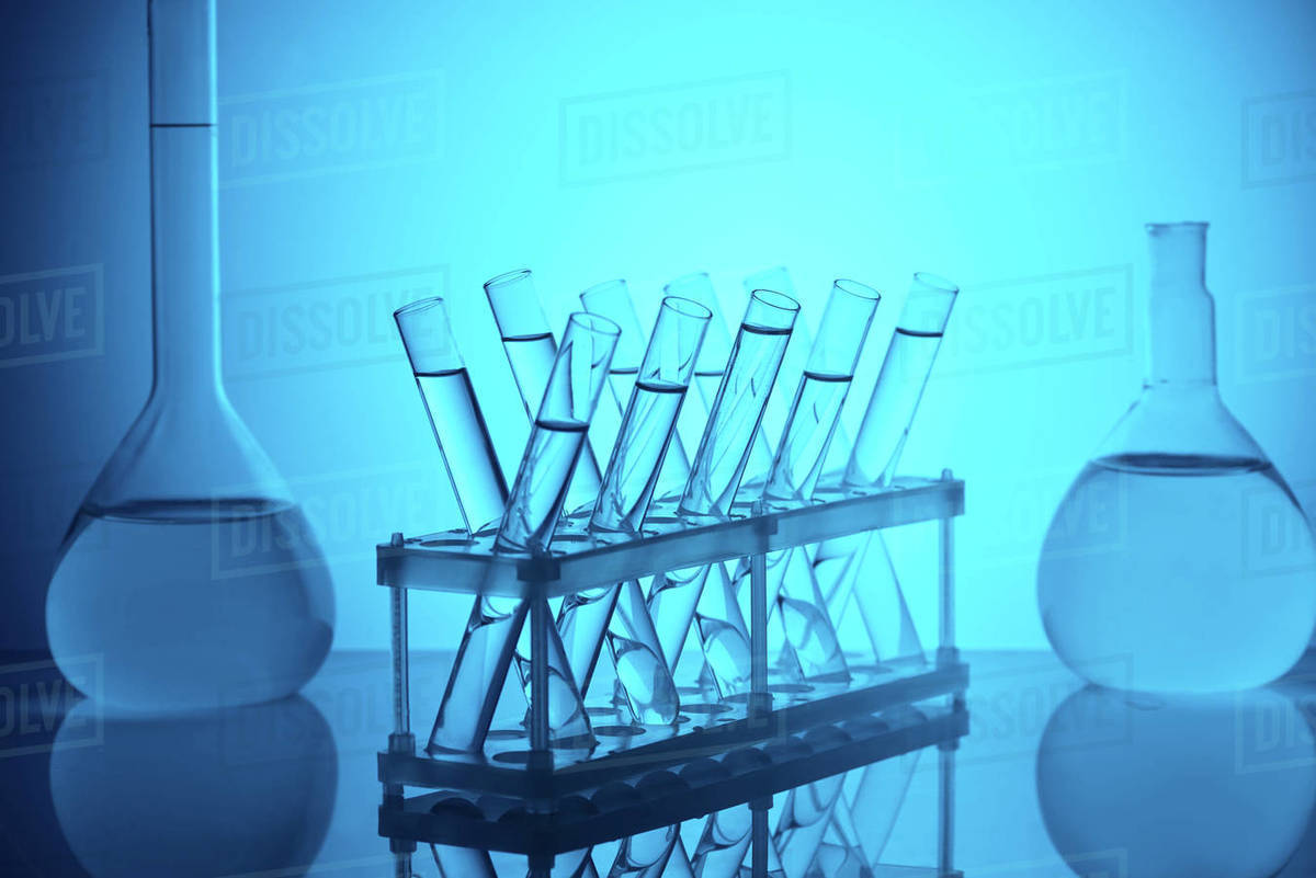 Glass tubes with liquid on stand and glass flasks on table on blue ...