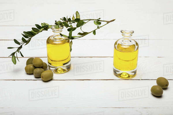 Close-up view of pure olive oil and green olives on wooden surface ...