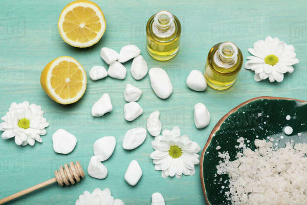 Top view of sea salt, oil in bottles, sliced lemon and chamomiles on ...
