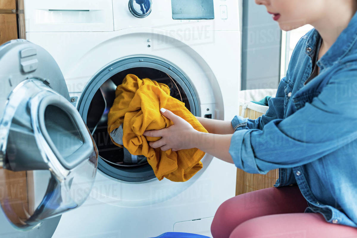 Cropped shot of young woman putting laundry into washing machine ...