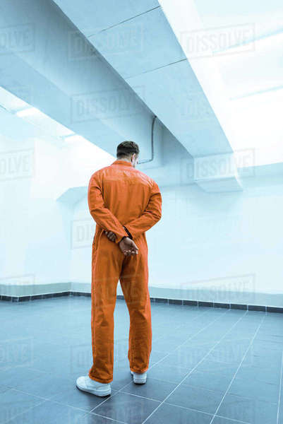 Rear view of prisoner in orange uniform standing in prison cell ...