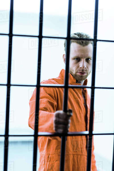 Prisoner holding prison bars and looking at camera - Stock Photo - Dissolve