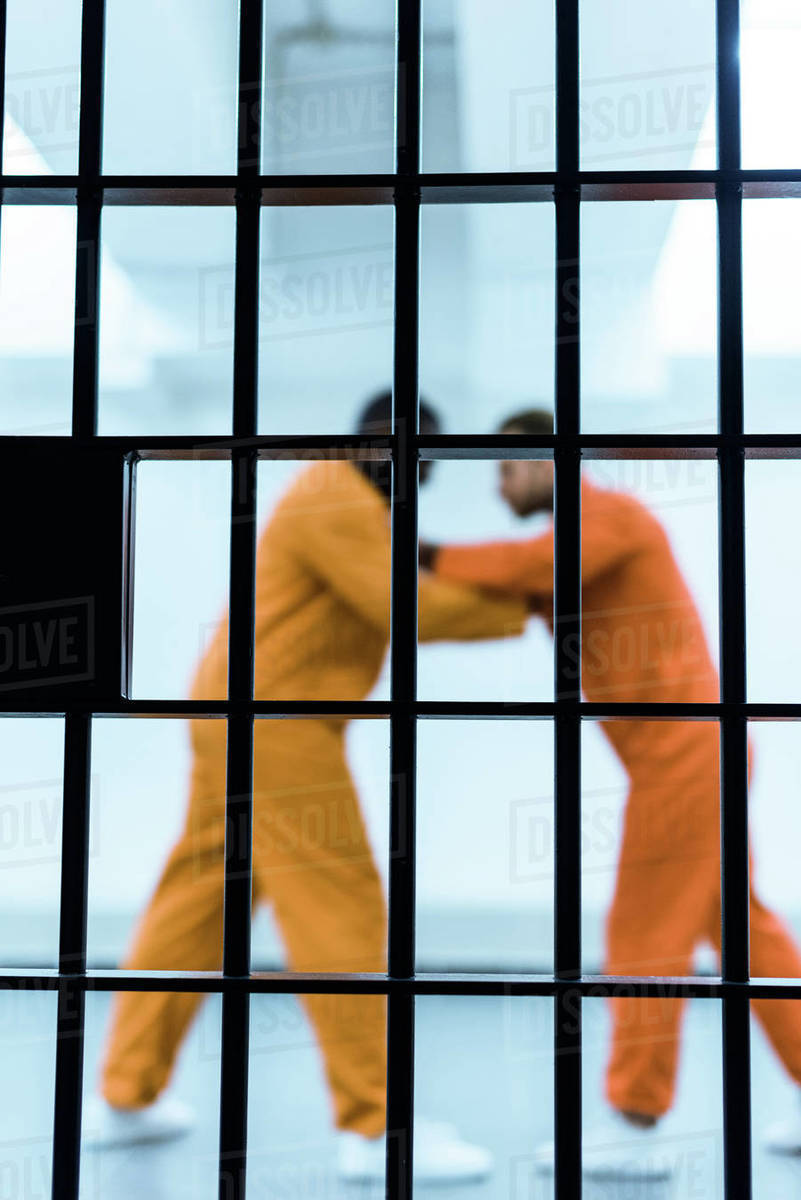 Side view of multiethnic prisoners threatening each other behind prison ...