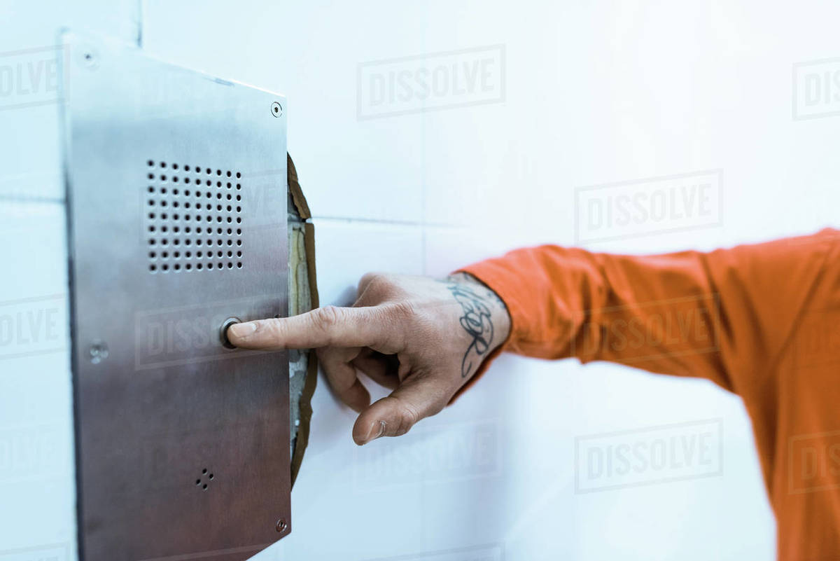 Cropped image of tattooed prisoner in orange uniform pressing button in ...