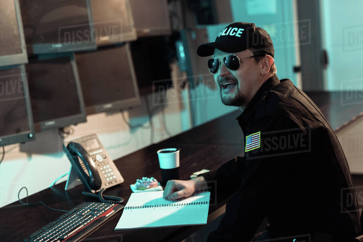 laughing prison guard sitting at working table and monitoring people in ...