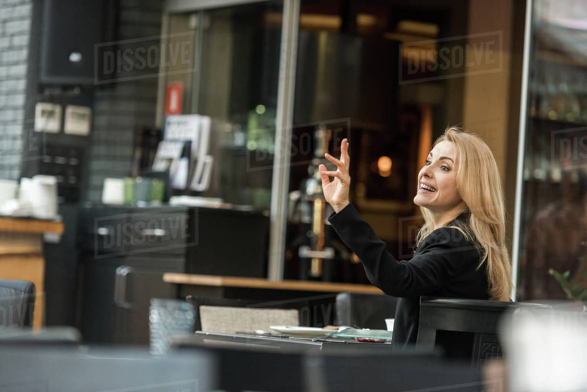 side view of smiling woman calling for waiter in restaurant - Stock ...