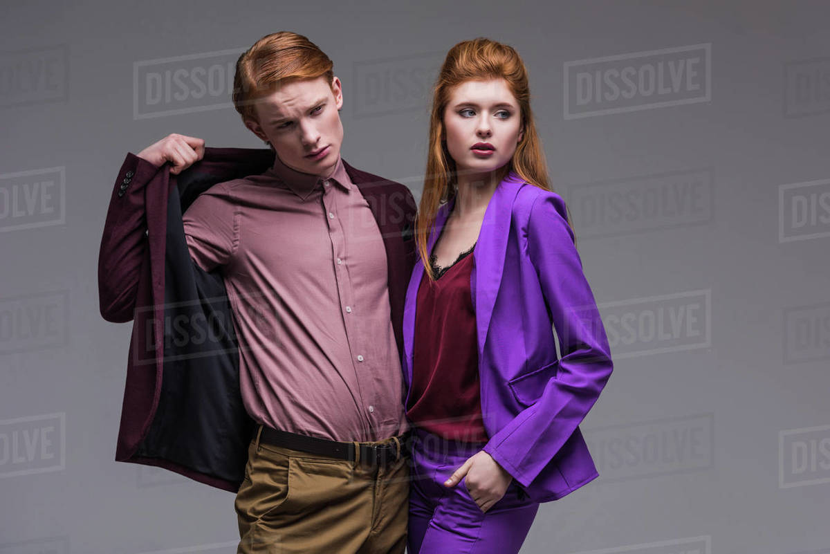 Couple of young fashion models dressed in formal wear isolated on grey ...