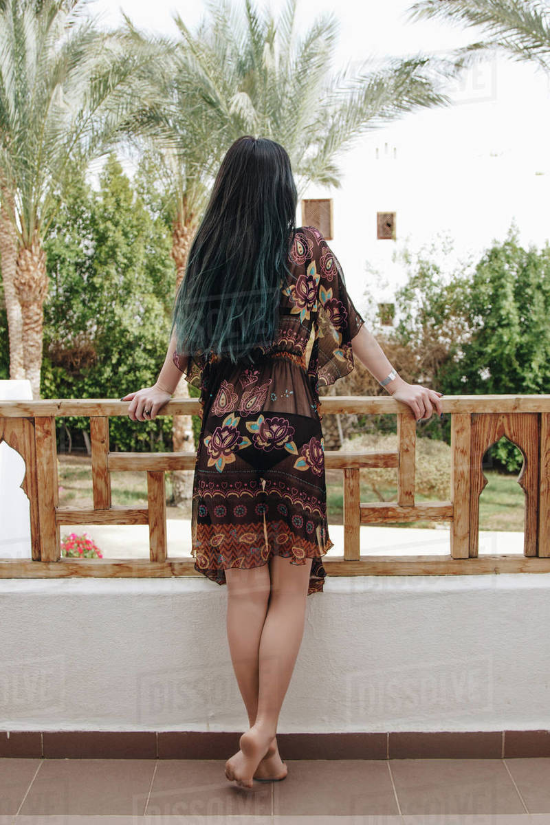 Back view of barefoot girl leaning at railing and looking at beautiful ...