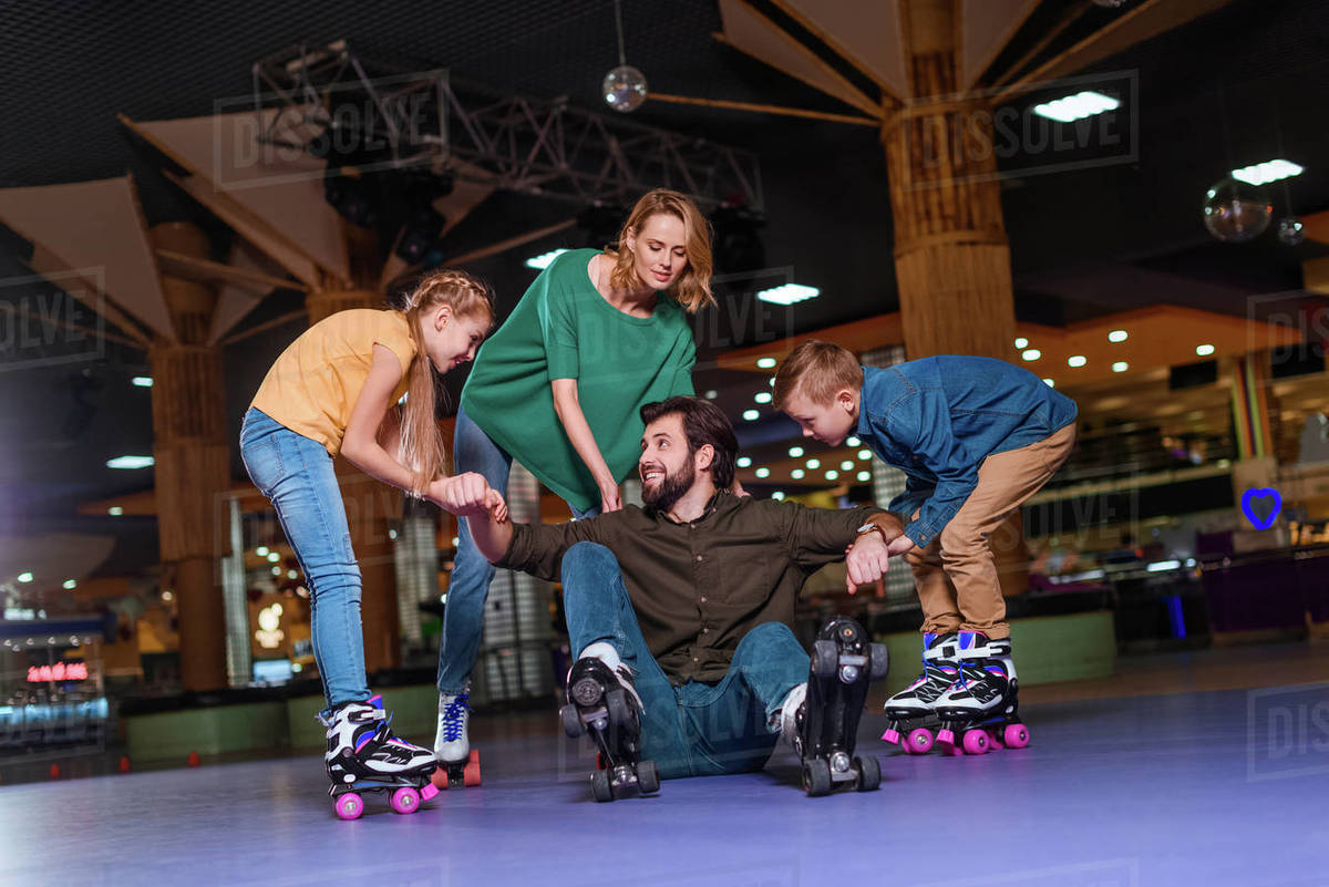 Family helping father in roller skates to get up on roller rink ...