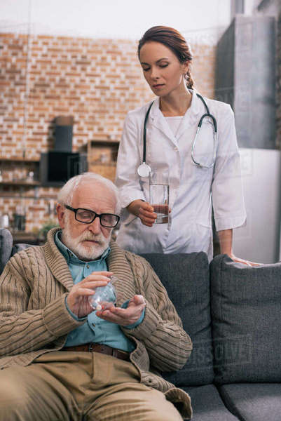 Doctor giving a glass of water to senior patient with pills - Stock ...