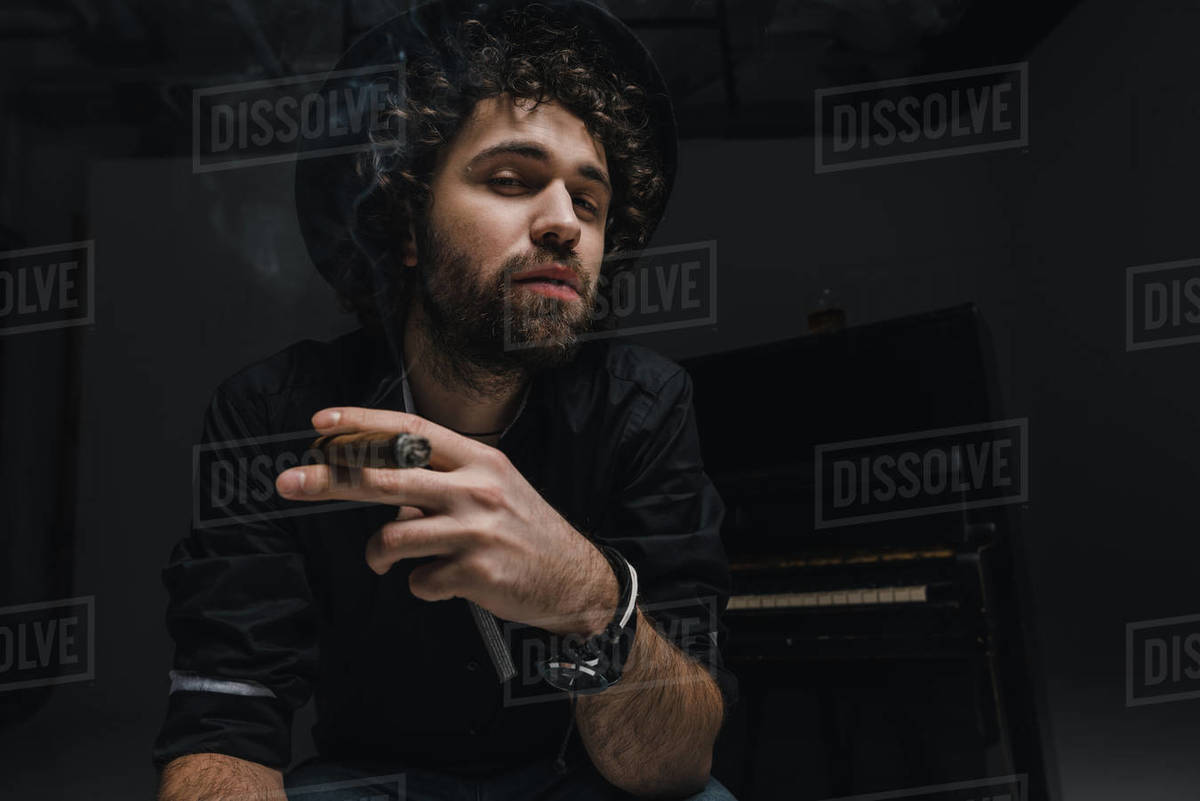 Serious musician smoking cigar in front of piano on black - Royalty ...