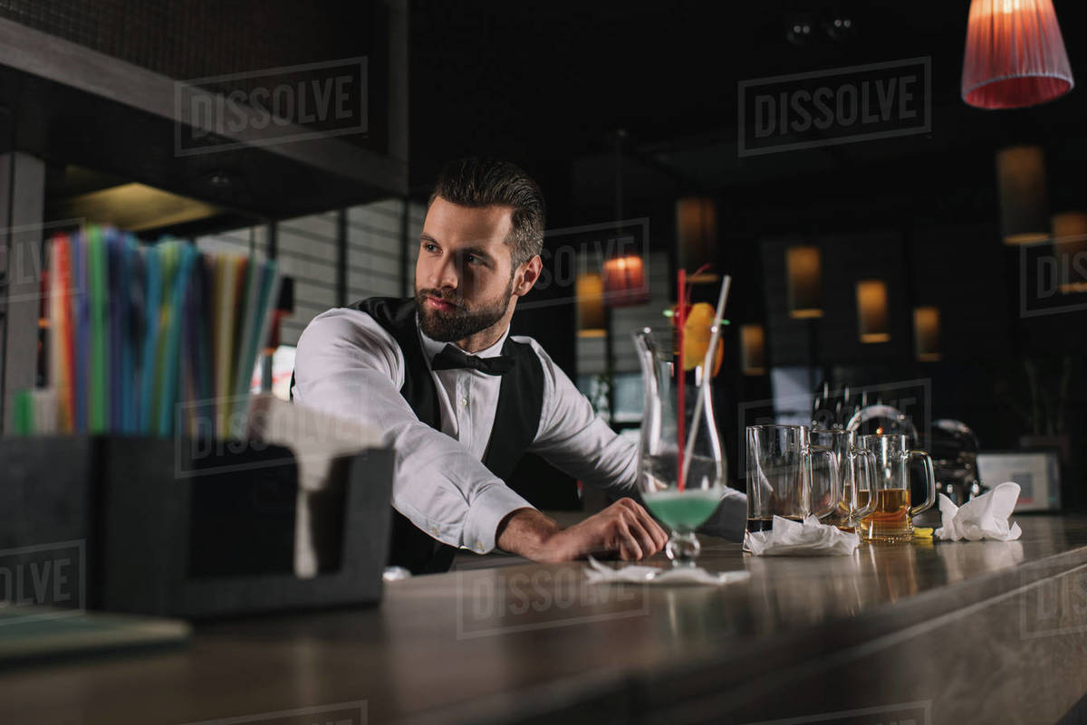 Handsome bartender leaning on bar counter and looking away - Royalty ...