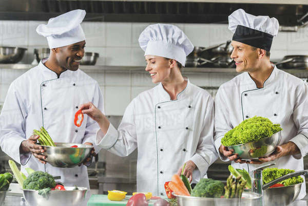 Happy multicultural chefs cooking vegetables at restaurant kitchen ...
