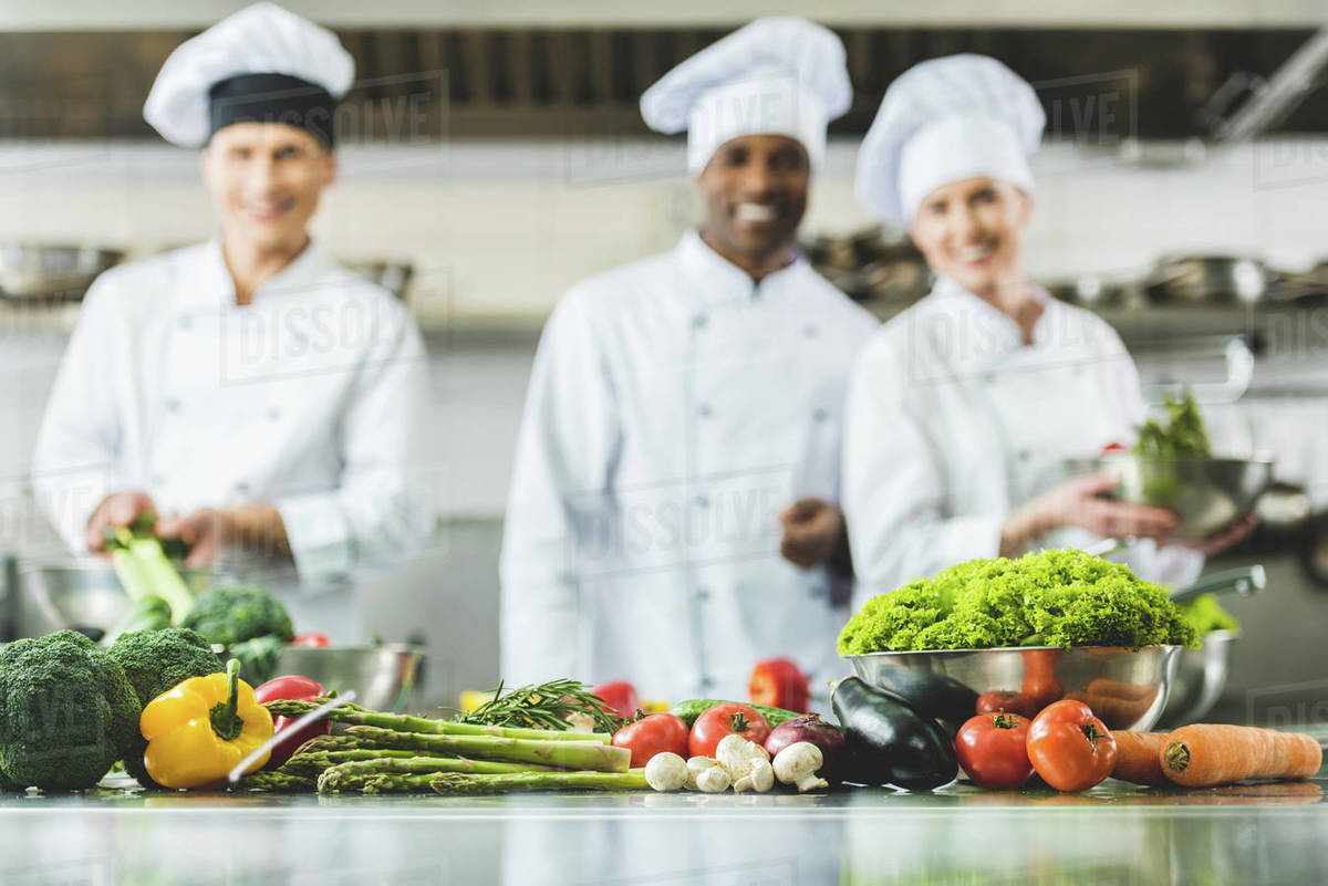 Smiling multicultural chefs at restaurant kitchen with vegetables on ...