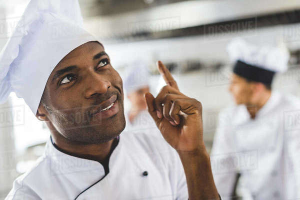 Handsome African American chef pointing up at restaurant kitchen ...