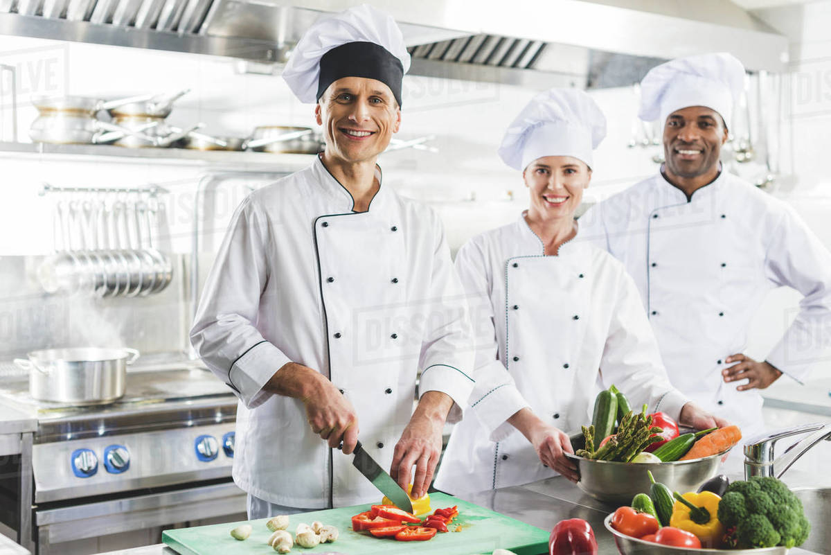 Smiling multicultural chefs looking at camera at restaurant kitchen ...
