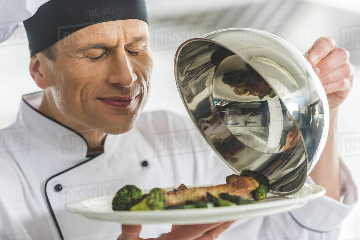 Handsome chef sniffing dish at restaurant kitchen with closed eyes ...
