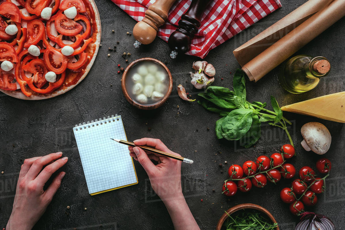 Cropped shot of woman writing notes while preparing pizza on concrete ...