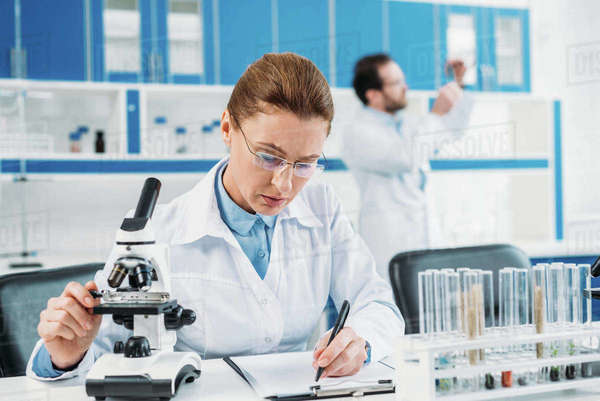selective focus of female scientist making notes in notepad at ...