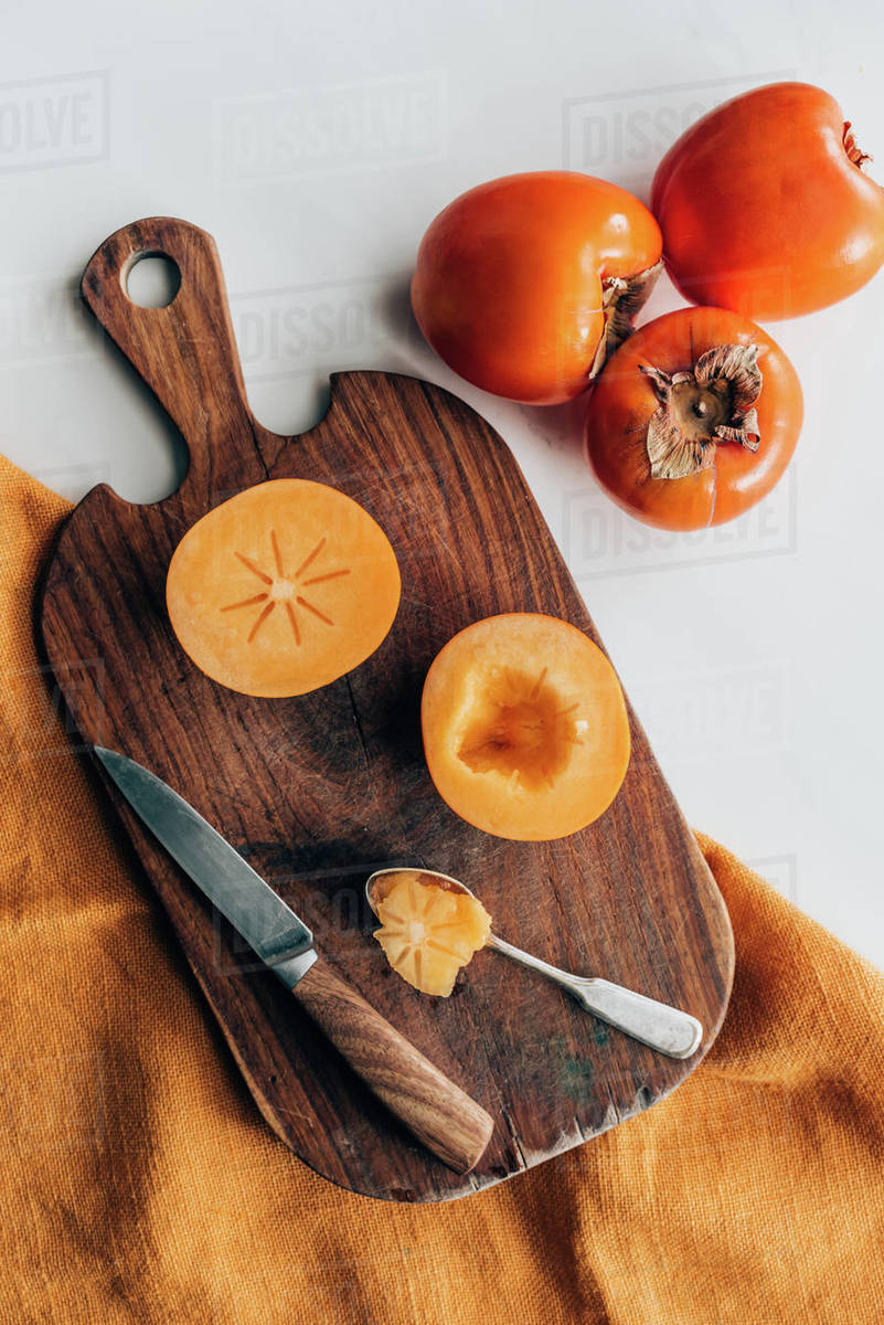 top view of persimmons on wooden board with knife and spoon - Royalty ...