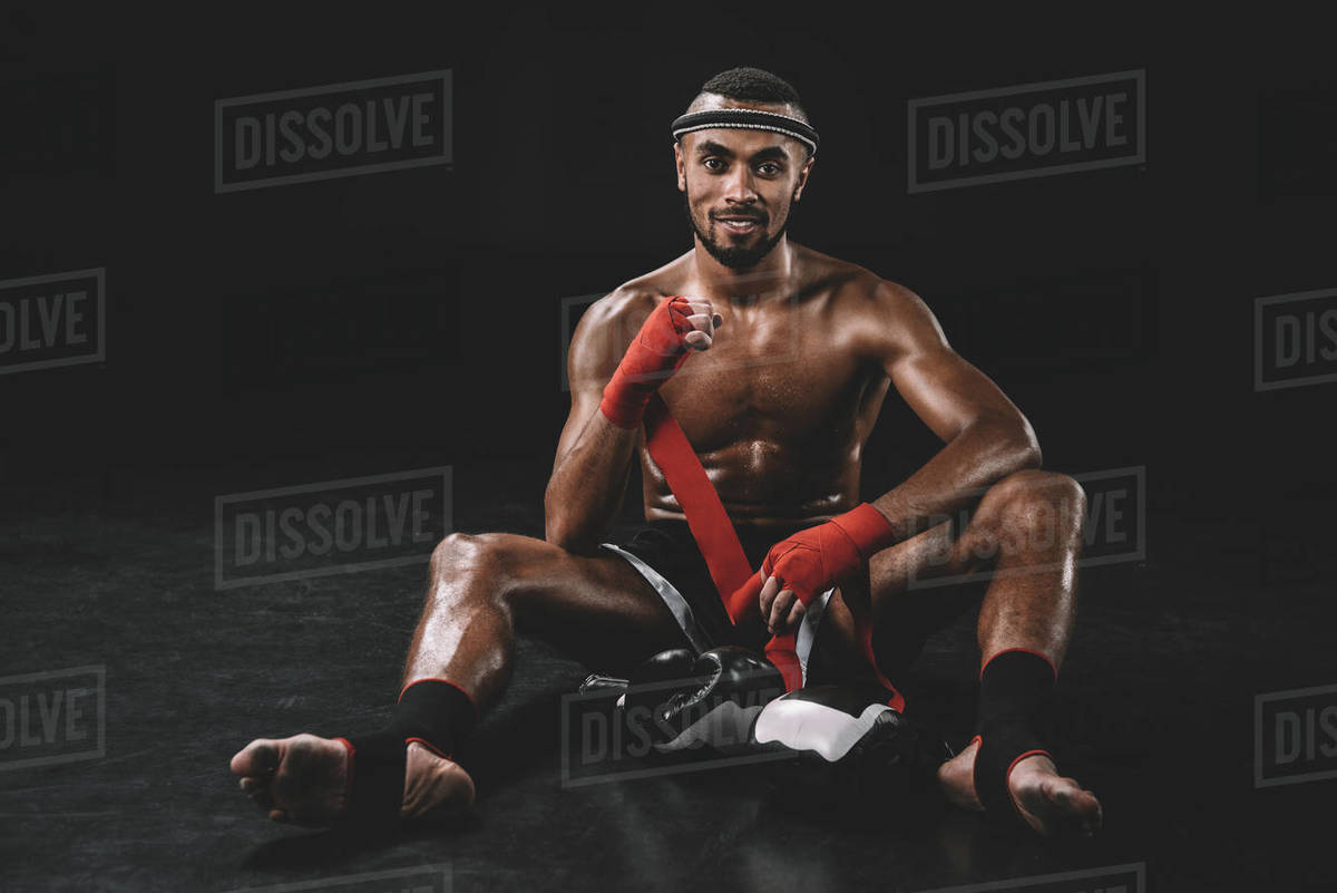 smiling muay thai fighter swathing hand in bandage isolated on black ...
