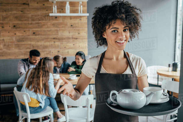 Smiling african american waitress holding tray with tea and customers ...