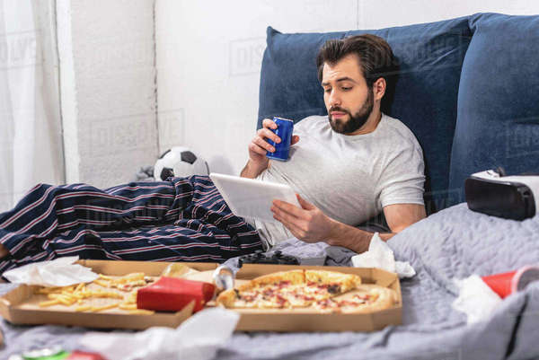 Handsome loner using tablet and holding drink on bed in bedroom - Stock ...