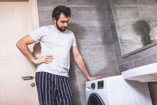 Handsome loner leaning on washing machine in bathroom - Royalty-free ...