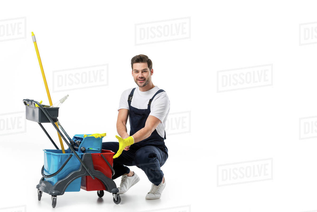Smiling cleaner in uniform and rubber gloves with cart isolated on ...