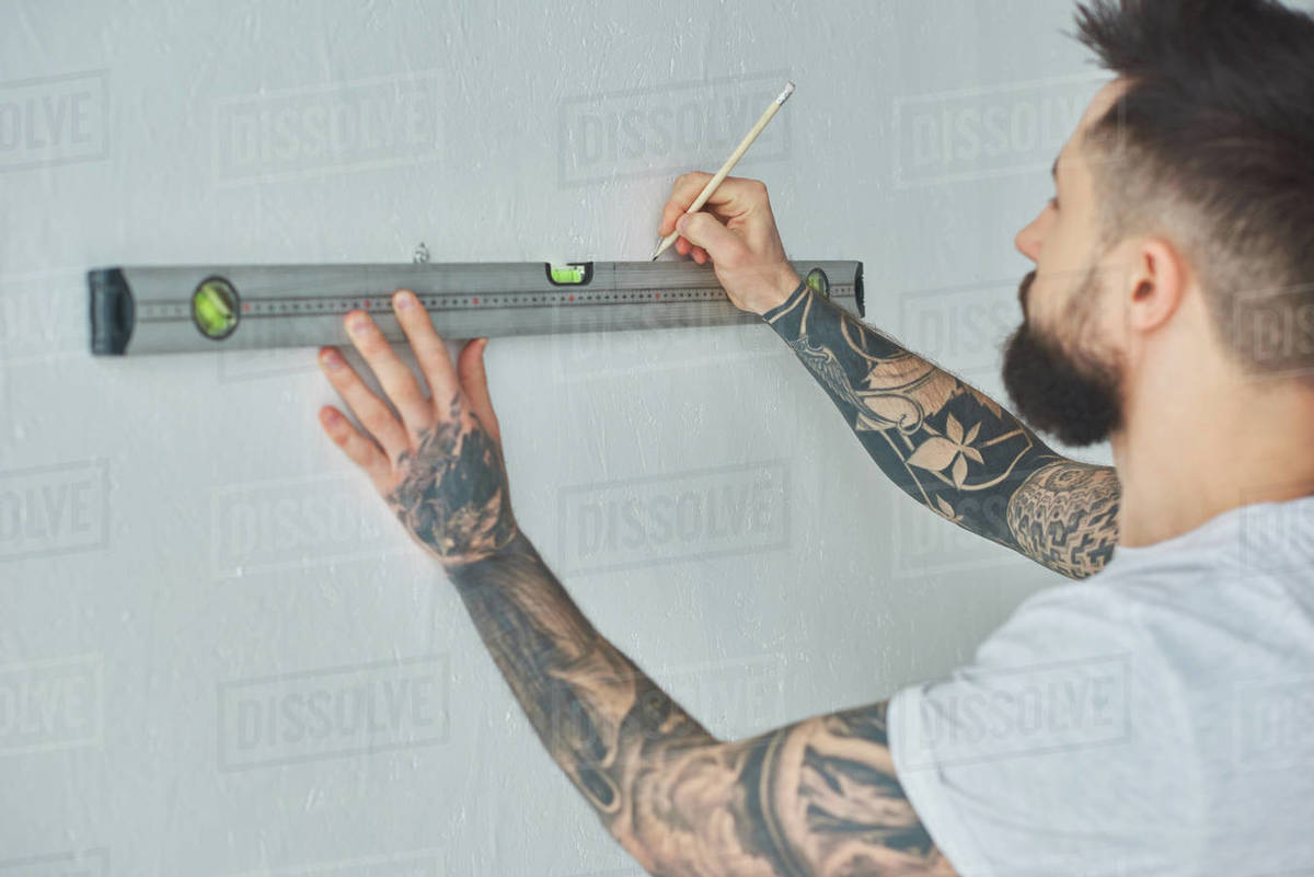 Cropped shot of young man holding level tool and marking wall with ...