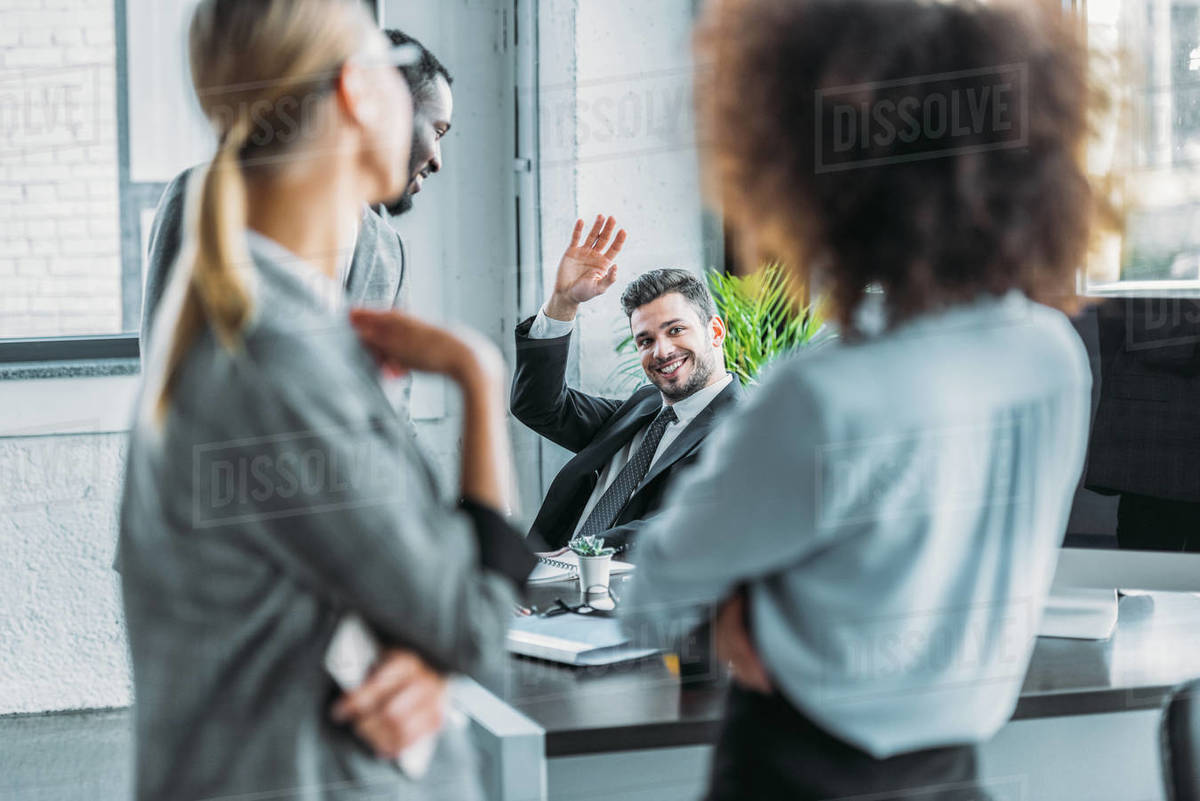 Smiling businessman waving hand to multicultural colleagues in office ...