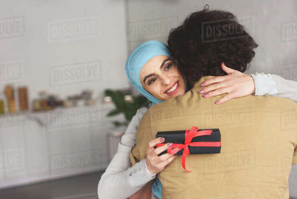 Muslim girlfriend in hijab hugging boyfriend and holding present at ...