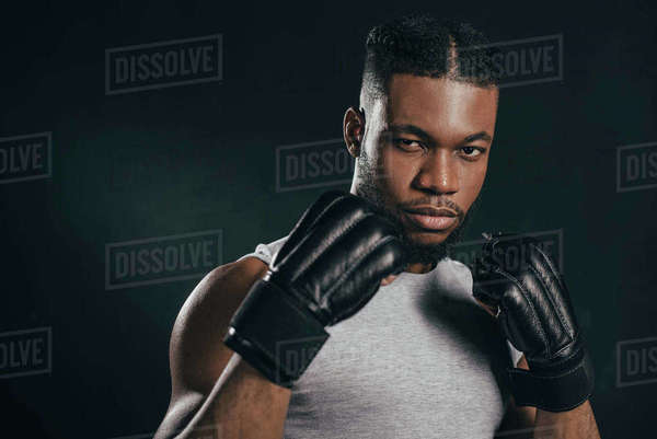 Serious young African American kickboxer in gloves looking at camera ...