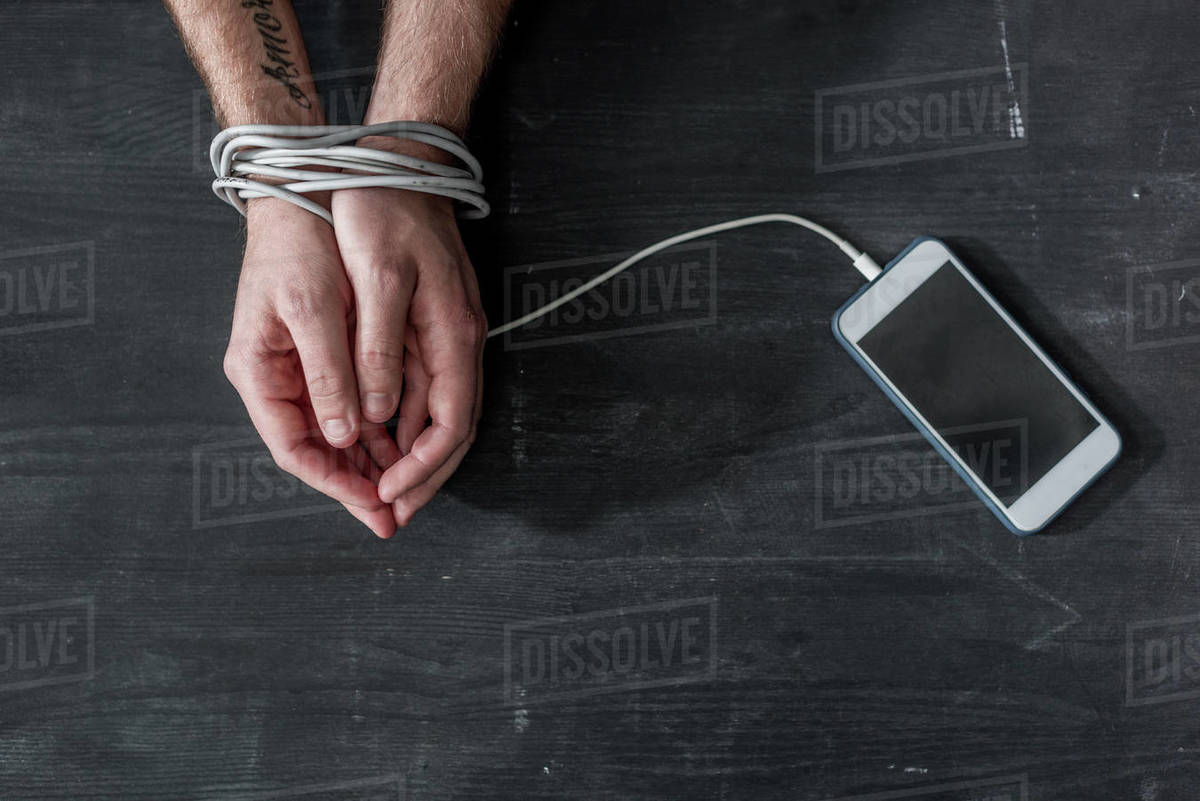 Cropped shot of man with hands tied with smartphone wire, phone ...