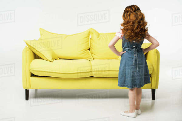 Rear view of stylish little child standing in front of couch isolated ...