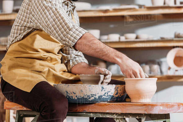 Cropped view of potter making ceramic pots on pottery wheel in workshop ...