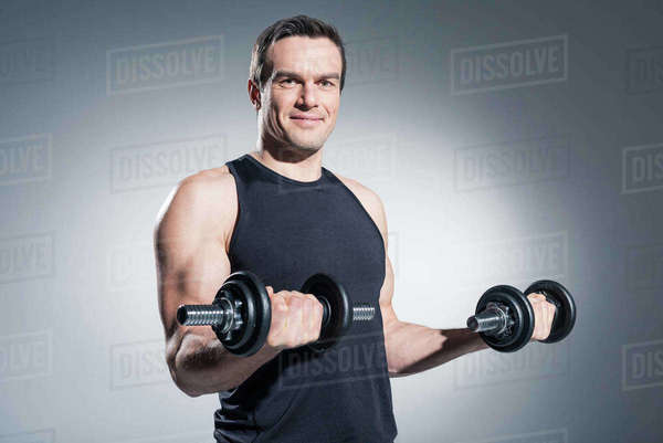 Smiling man lifting dumbbells on grey background - Stock Photo - Dissolve
