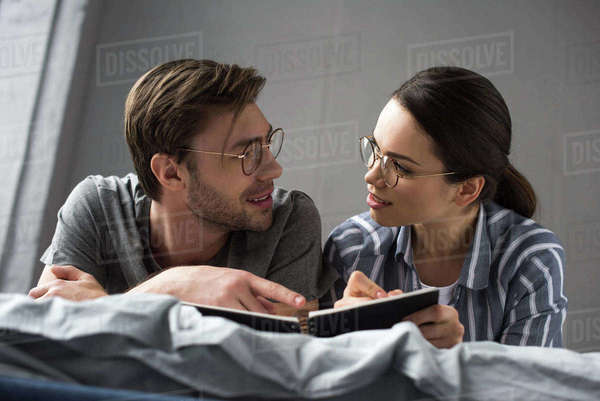 Young attractive couple writing in notepad while lying in bed - Royalty ...