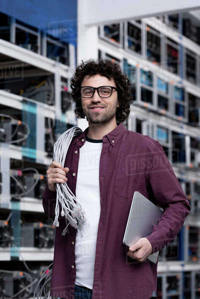 Handsome young computer engineer with laptop and wires working at ...