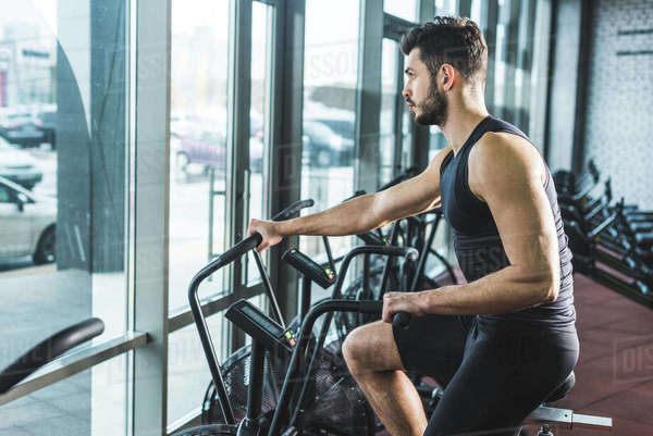 Side view of young sportsman doing workout on exercise bike in sports ...