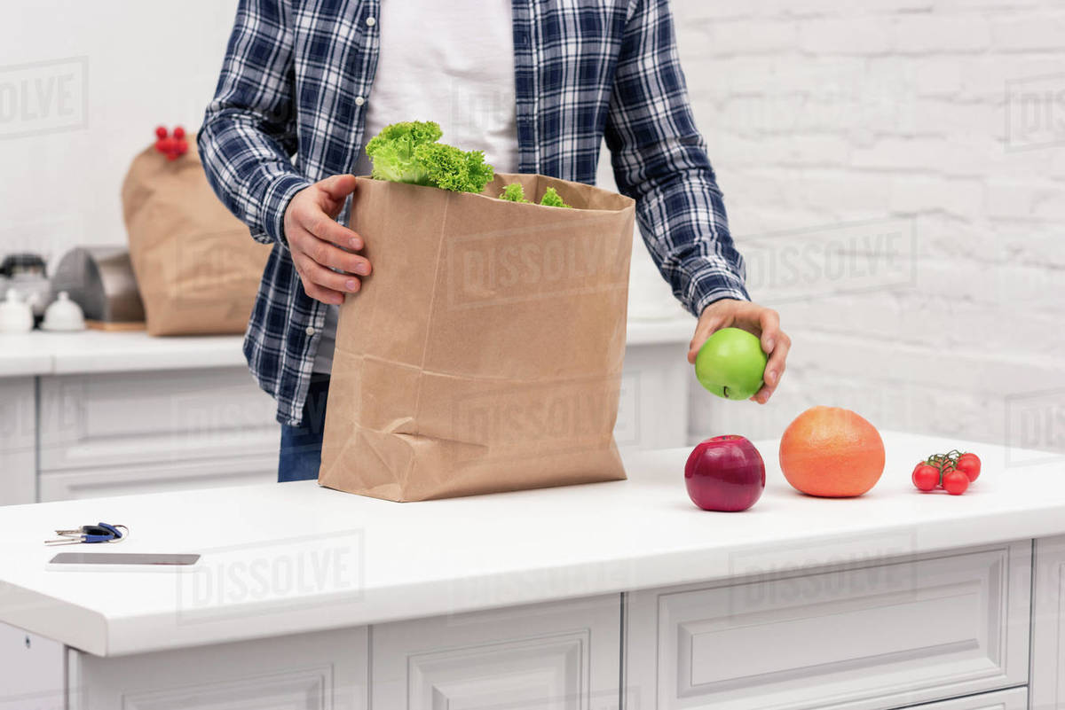 Cropped shot of man unpacking grocery store paper bag at kitchen ...
