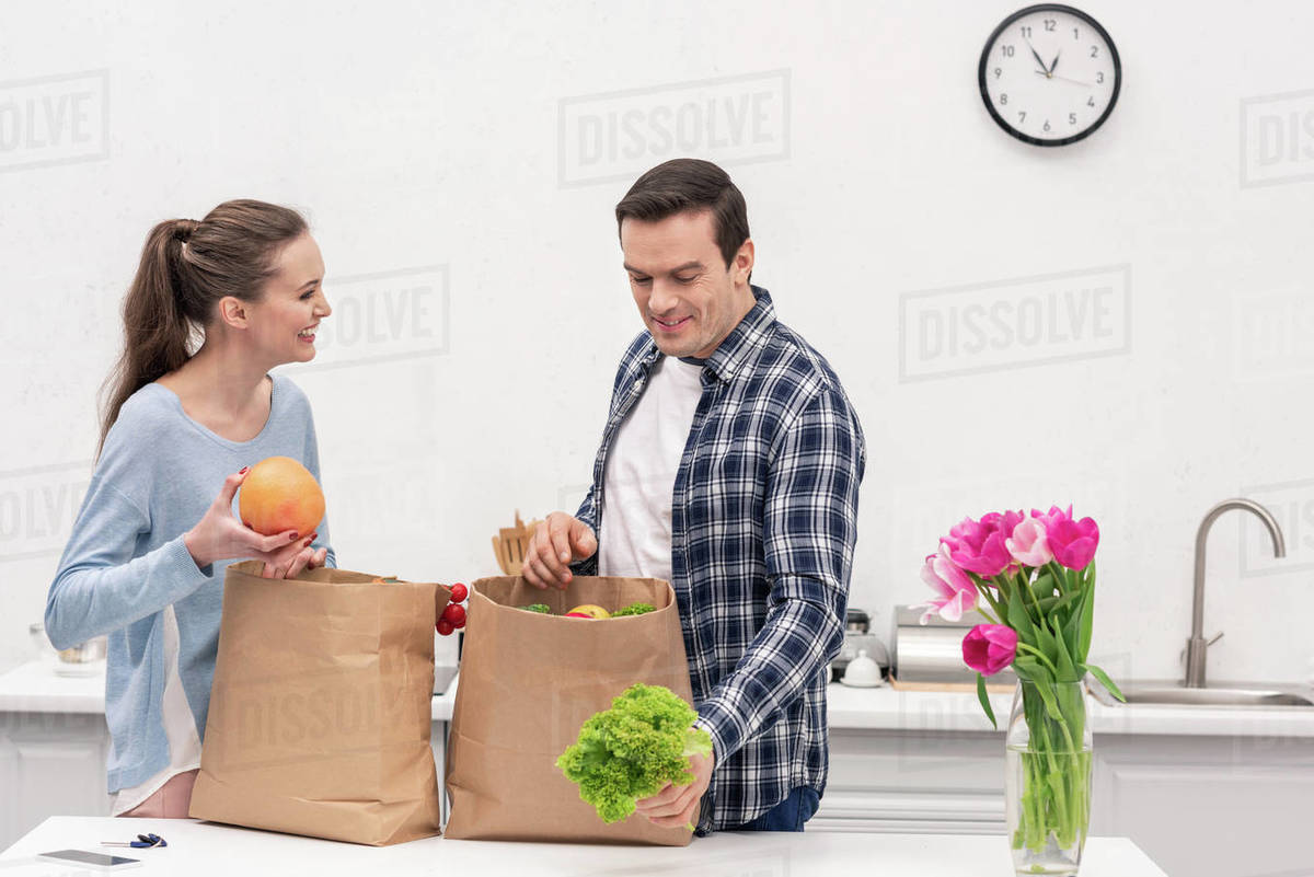 Beautiful adult couple taking vegetables and fruits out of paper bags ...