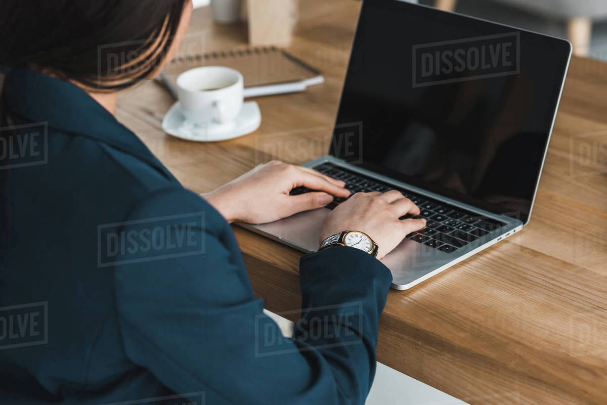 Rear view of businesswoman typing on laptop by table in office - Stock ...
