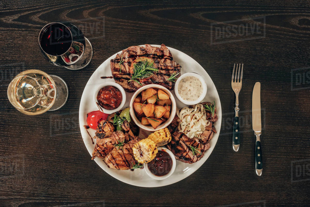 Top view of plate with beef steaks, chicken wings and wine on wooden ...