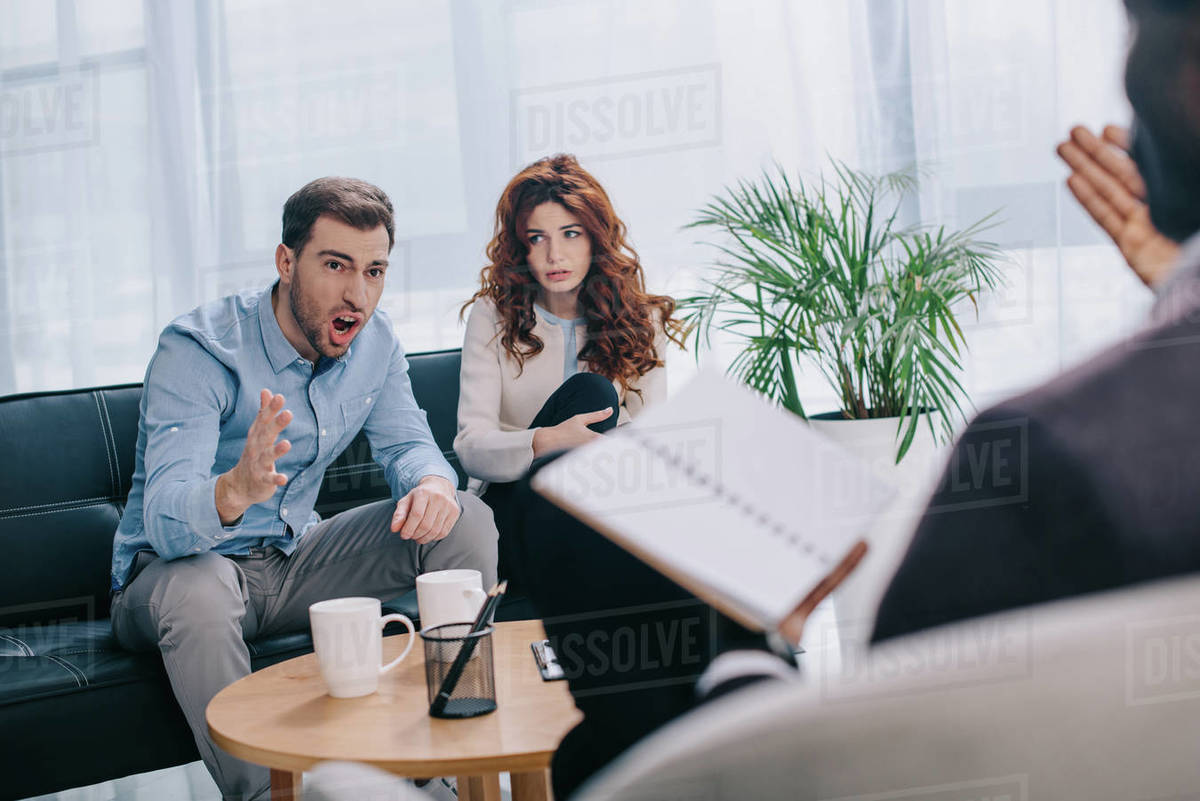 Angry young man with girlfriend sitting on sofa and arguing with ...